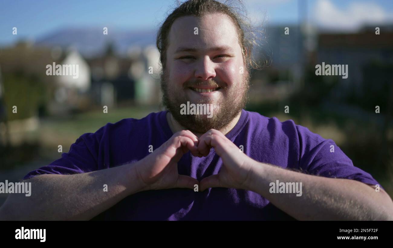 One young overweight man doing heart sign with hands outside. Happy ...