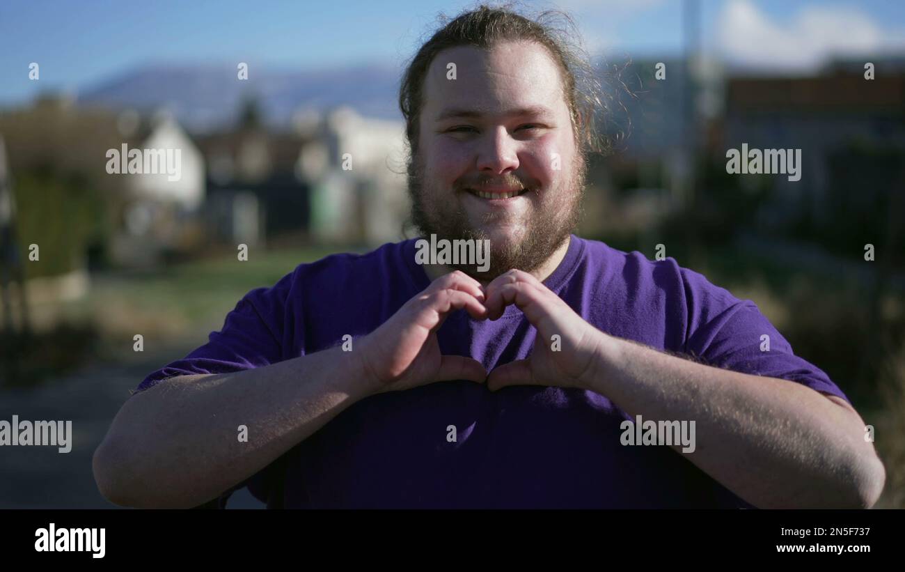 One young overweight man doing heart sign with hands outside. Happy ...