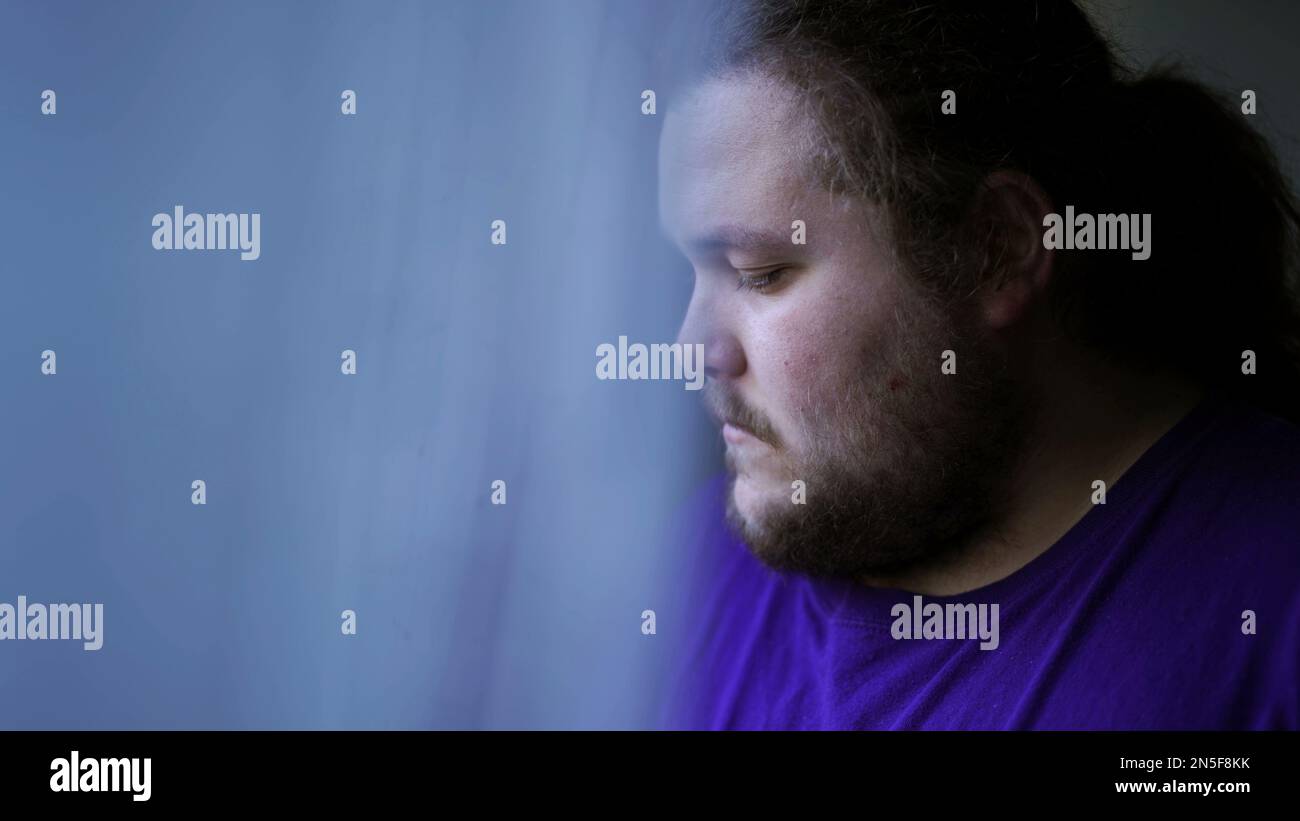 One contemplative overweight man standing by window looking outside by ...