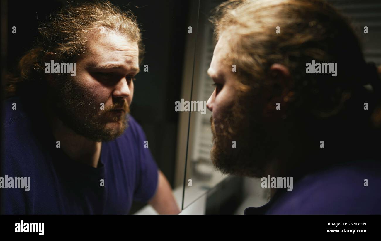 One desperate young man suffering from stress in front of mirror ...