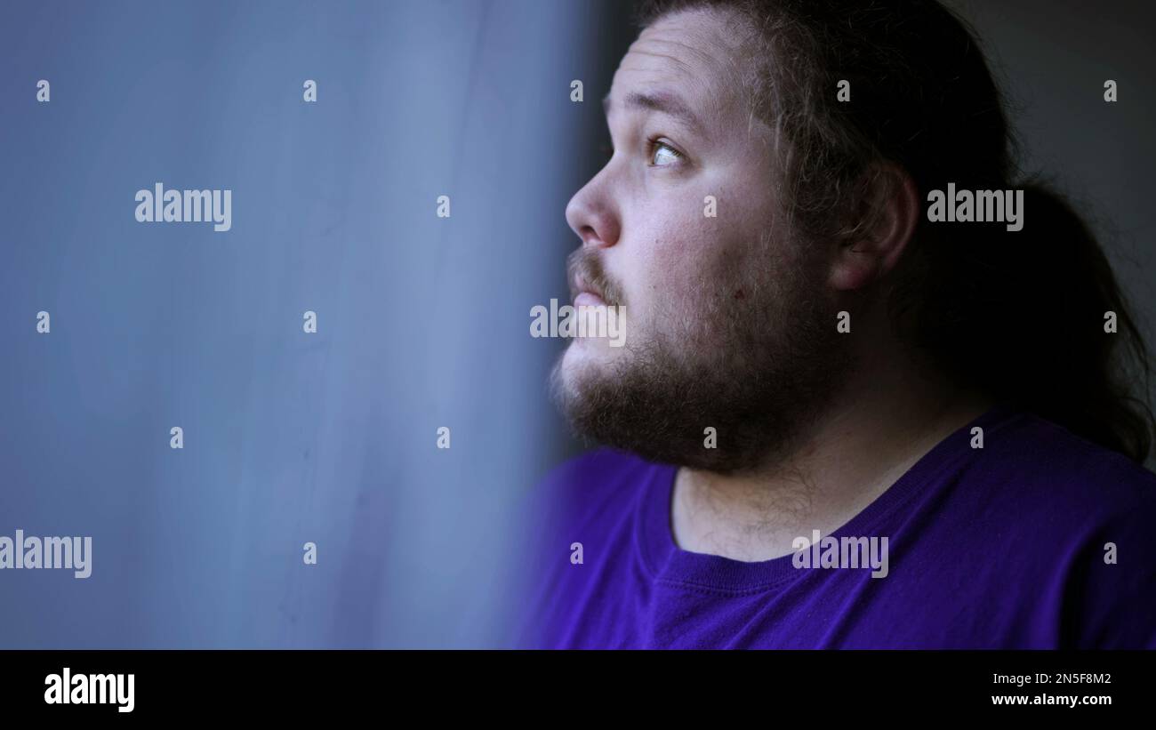One contemplative overweight man standing by window looking outside by ...