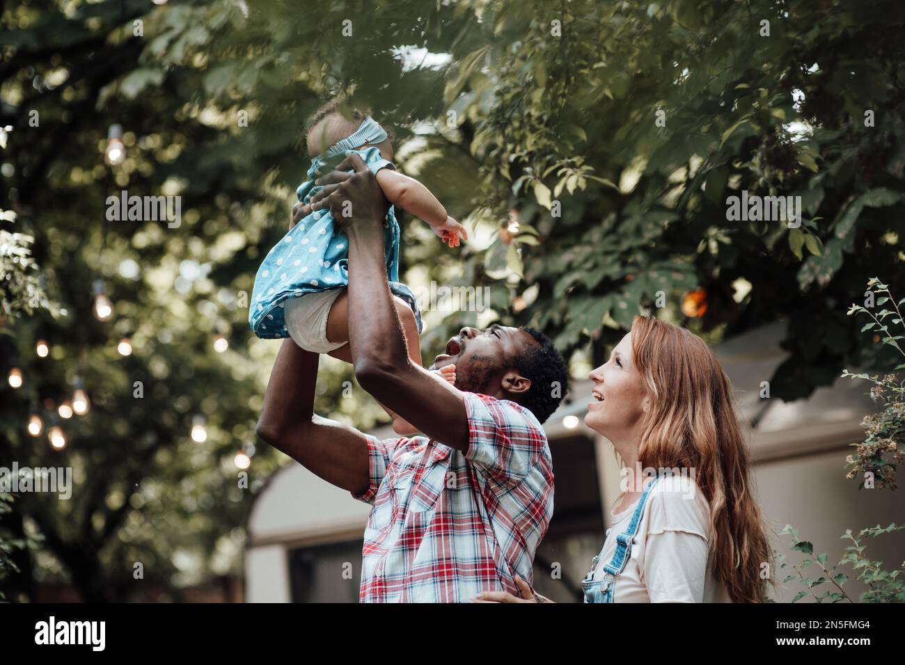 Mixed race family hold dark skinned infant daughter in air spend time ...