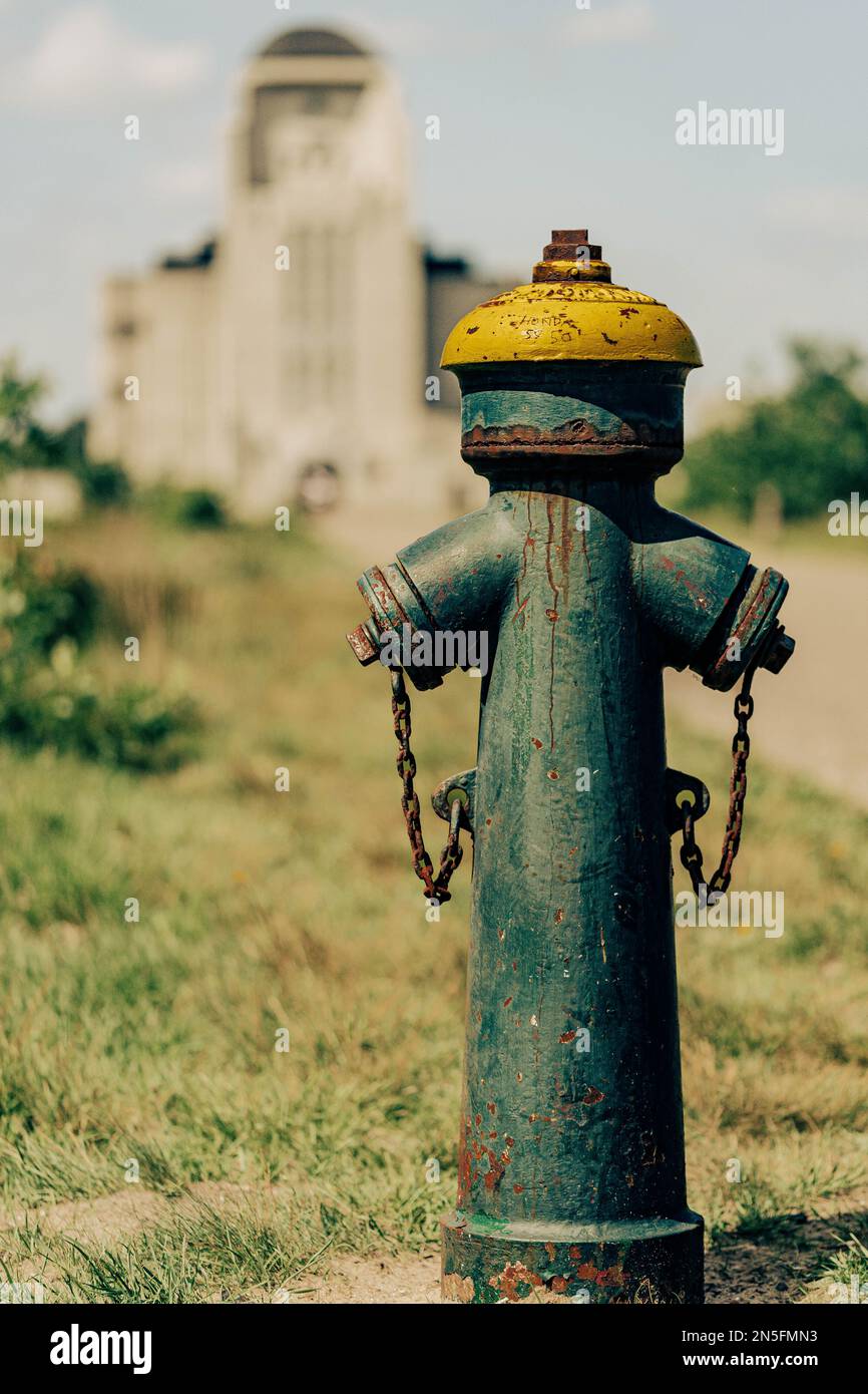 An old rusty fire hydrant on the grass in the park with a building in ...