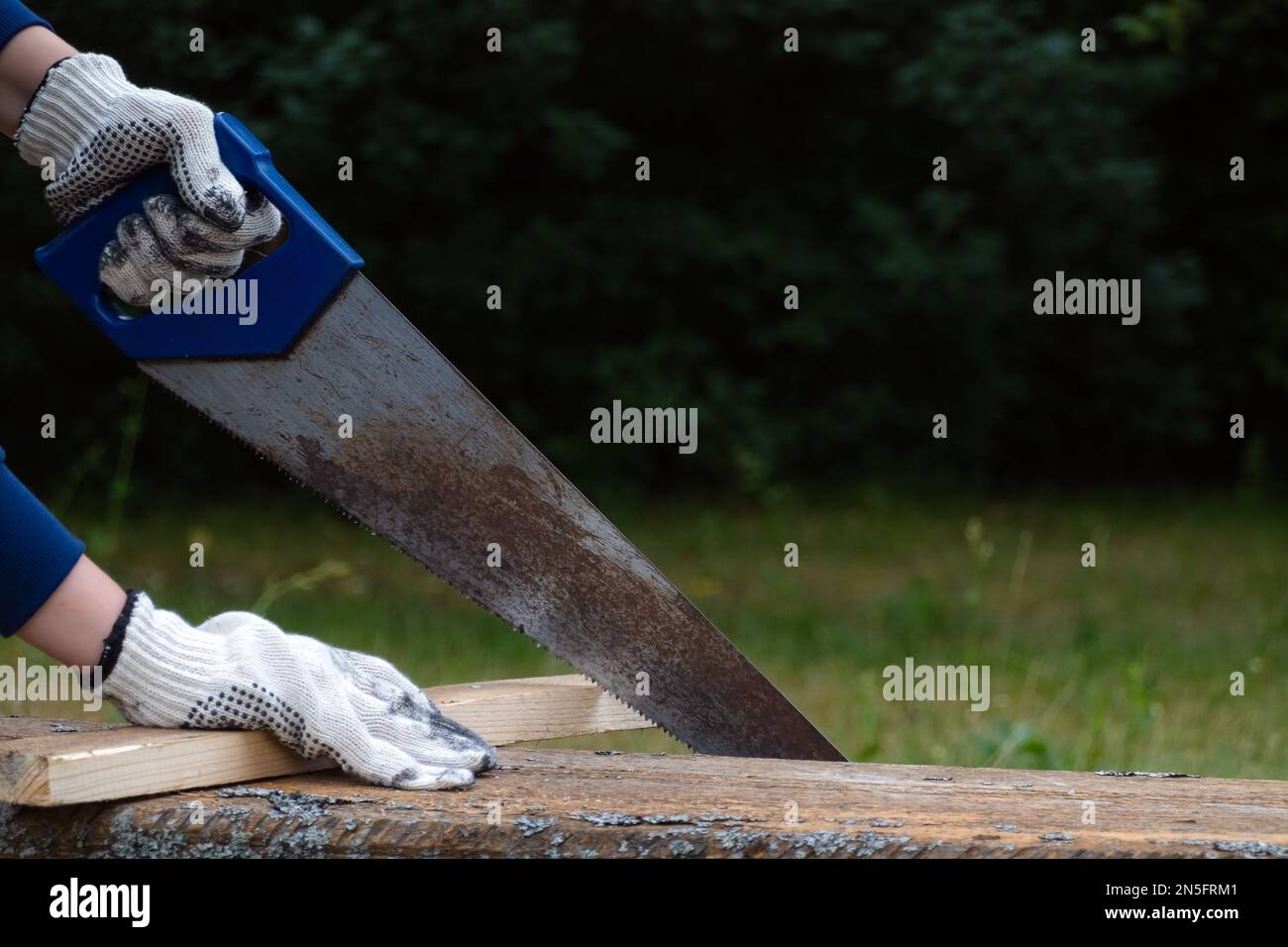 Close up of carpenter wearing gloves and hand sawing wooden plank with ...