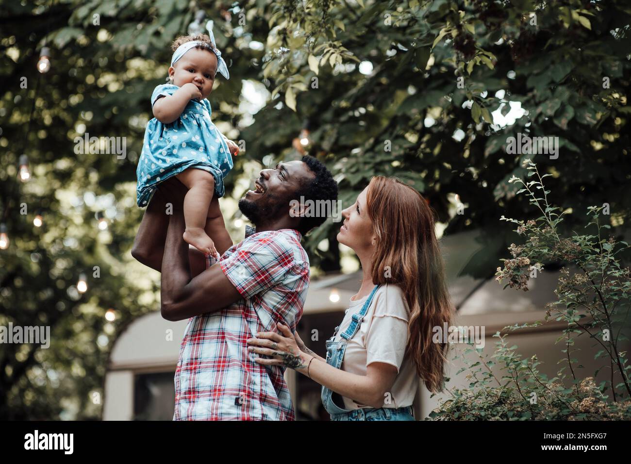 Mixed race family hold dark skinned infant daughter in air spend time ...