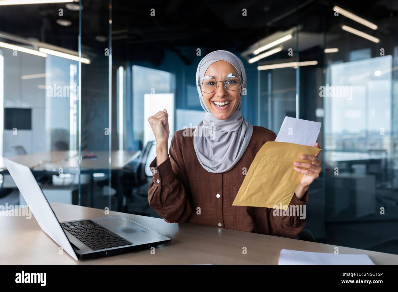 A young woman, an Arab student in a hijab, sits at the table, holds an ...