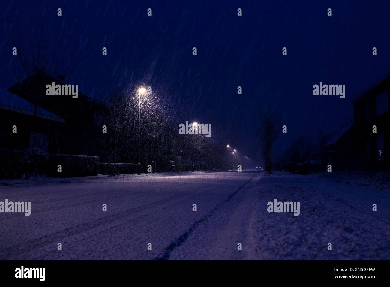 A wide dark night portrait of a snowy street during heavy snowfall with ...