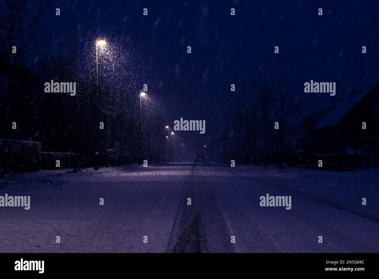 A dark night portrait of a snowy street with snow flakes still falling ...
