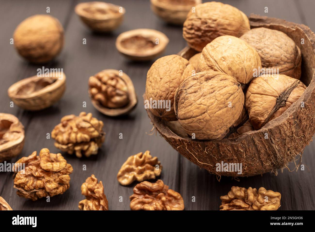 Whole walnuts in coconut shells. Walnut kernels and shells on table. Dark wooden background ...