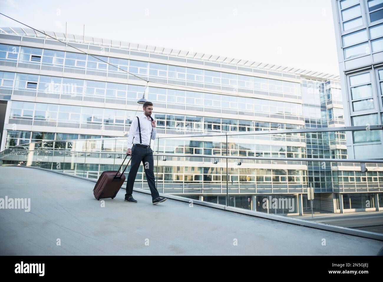 Businessman pulling wheeled luggage on footbridge, Munich, Bavaria ...