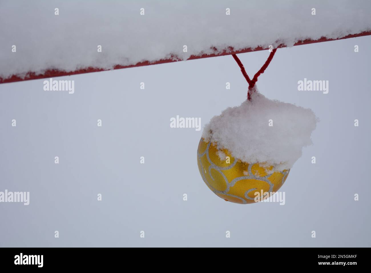 Snow covered christmas ball ornament hanging from snowy bridge rail ...