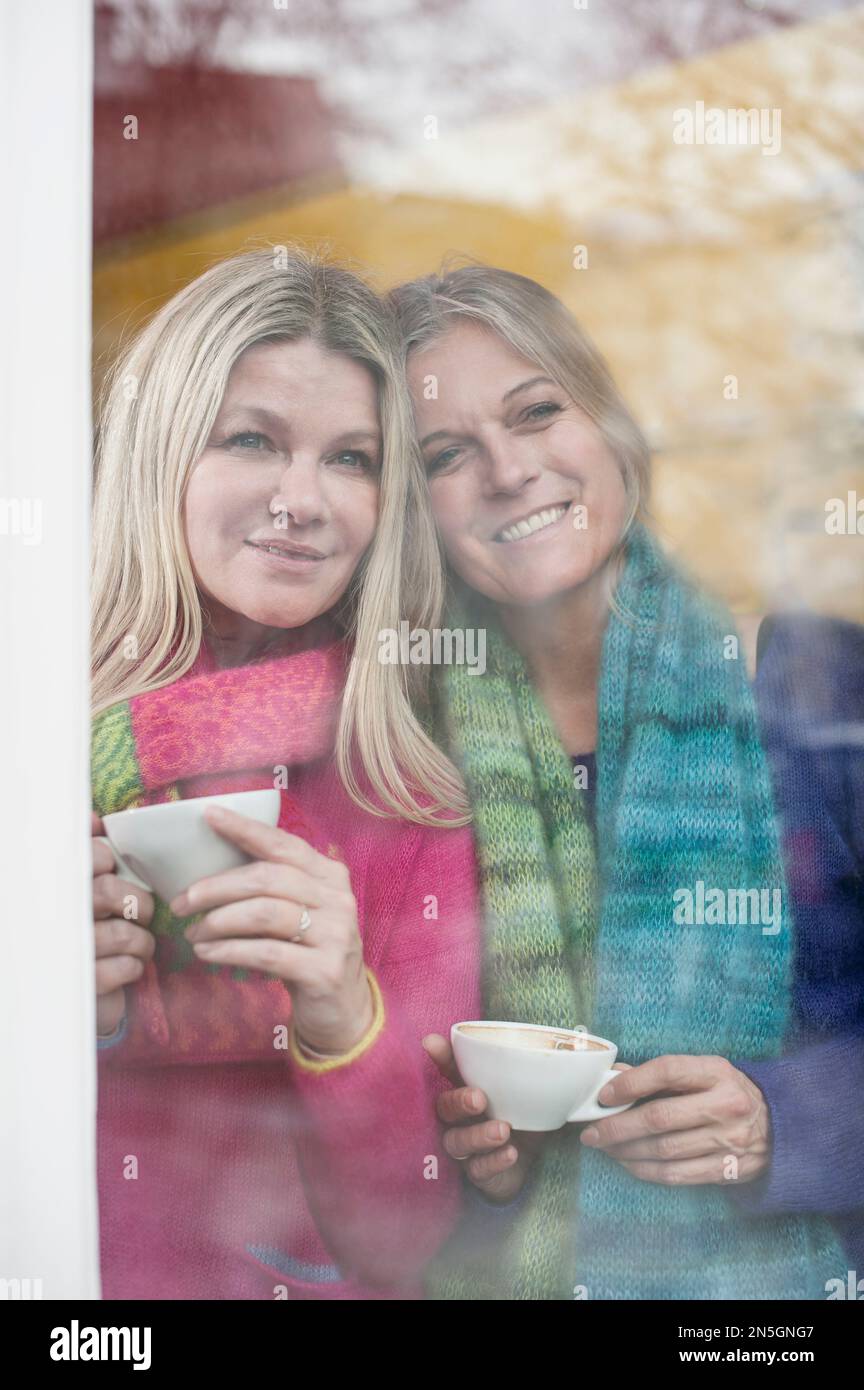 Two friends looking through window and drinking coffee in coffee shop ...