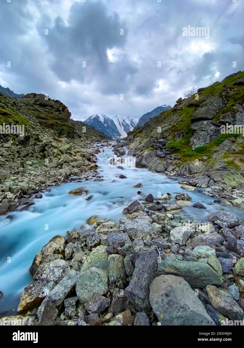 Alpine stream flows over stones near mountains with glaciers and snow ...