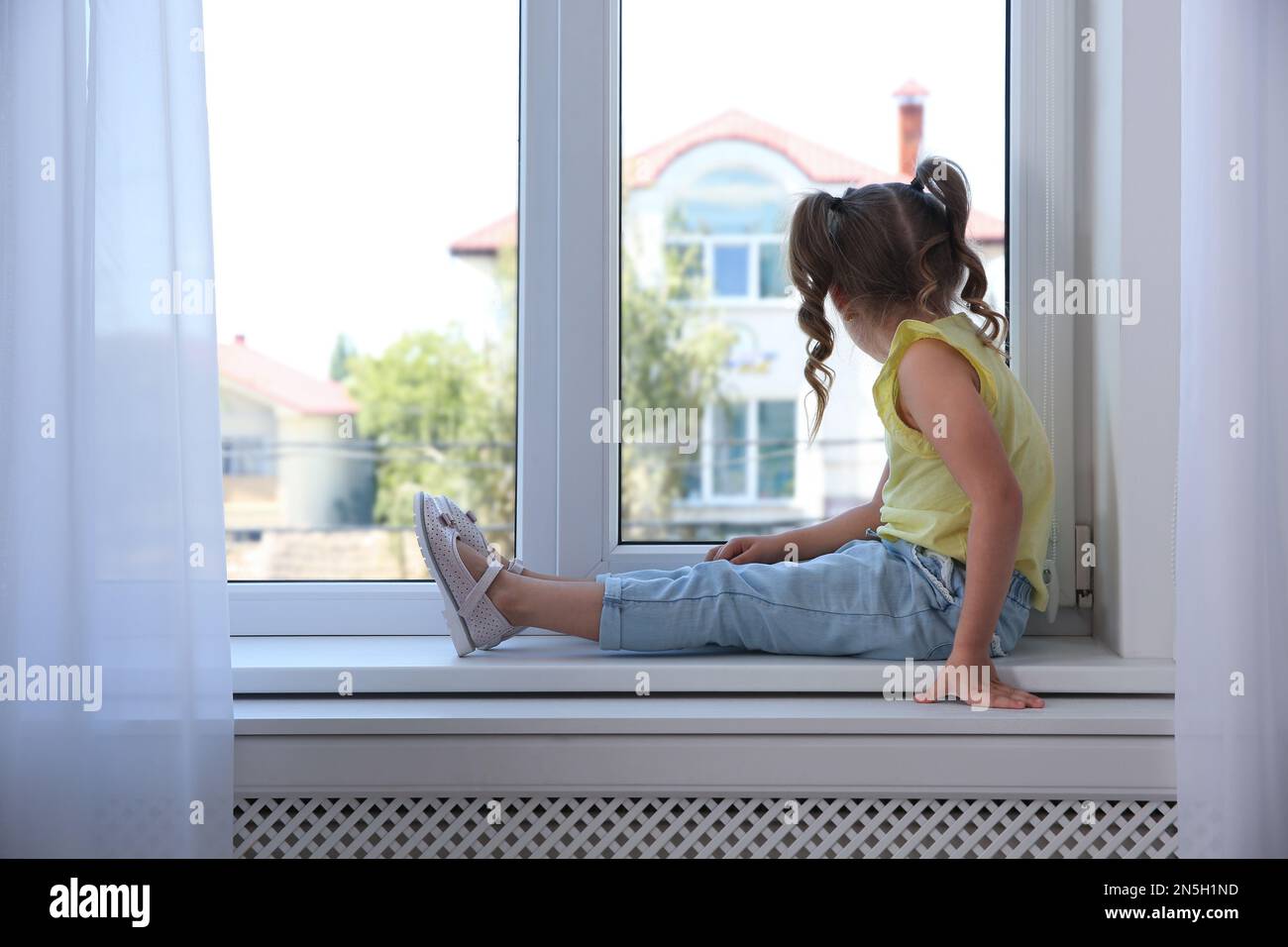 Cute little girl on window sill at home Stock Photo - Alamy