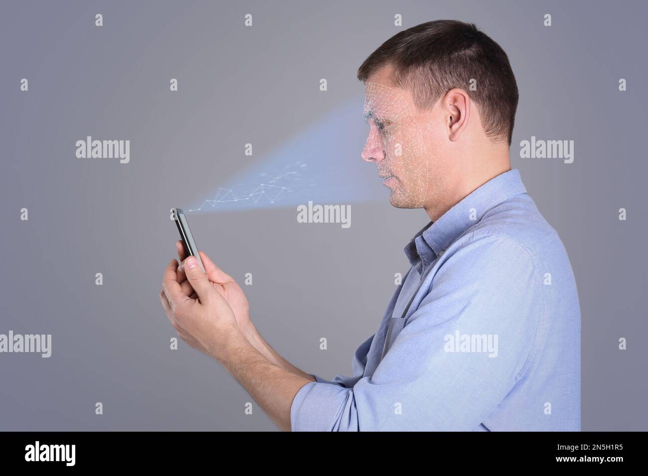 Man unlocking smartphone with facial scanner on grey background ...