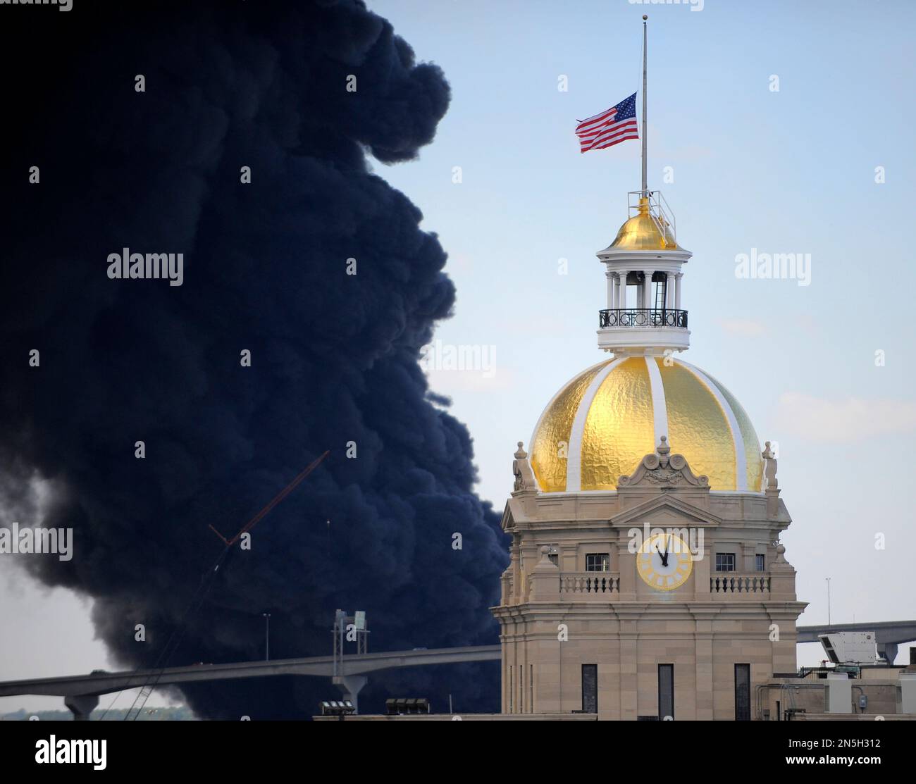 A black column of smoke rises hundreds of feet into the air behind ...