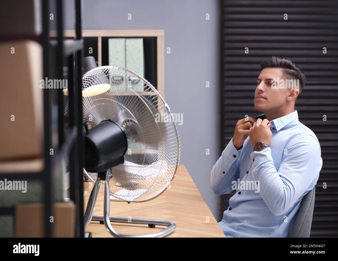 Man enjoying air flow from fan at workplace Stock Photo - Alamy