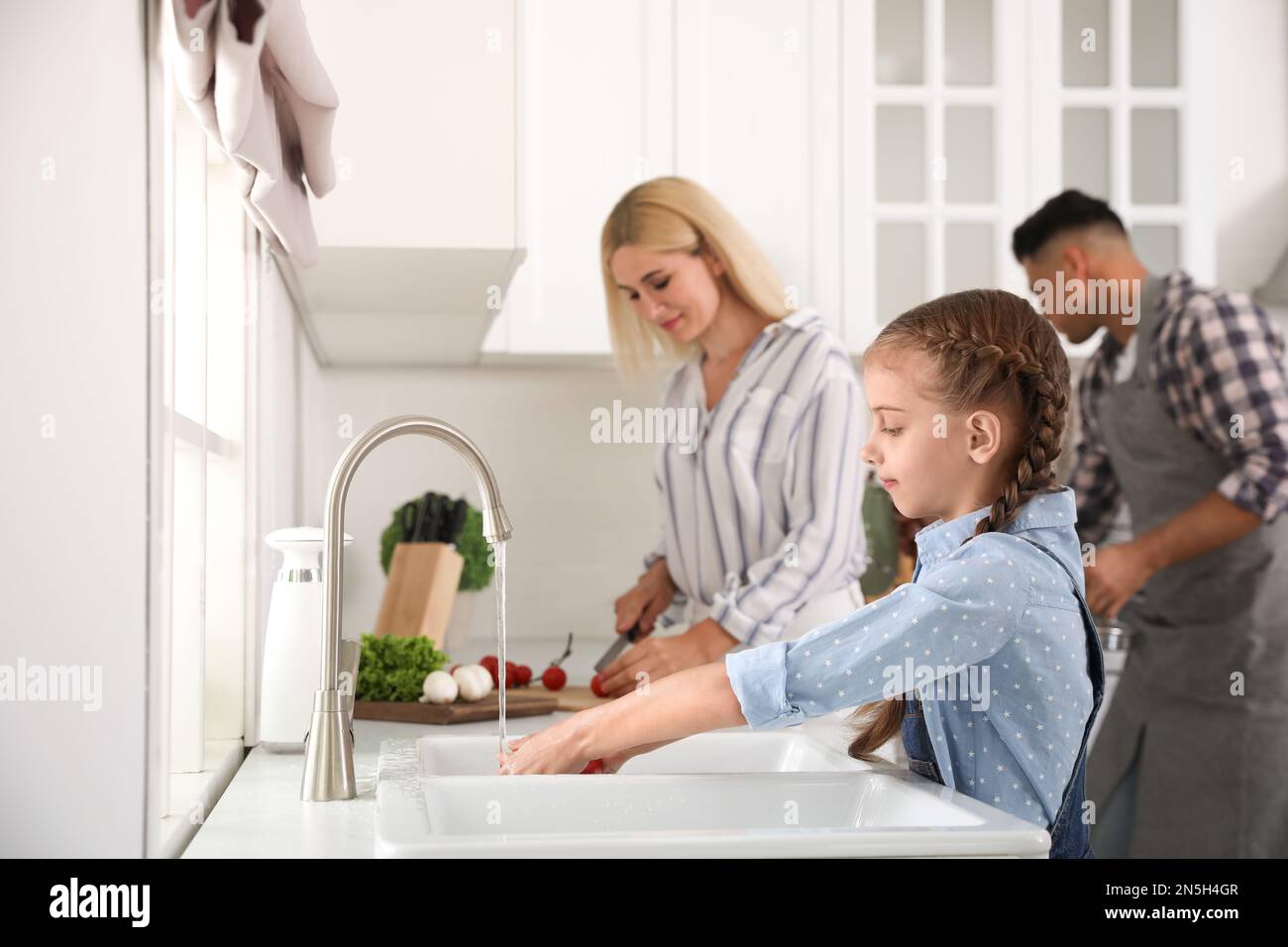 Little girl washing vegetables and her parents in modern kitchen Stock ...