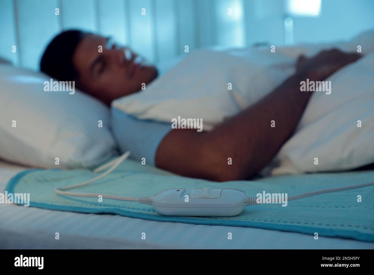 Man sleeping in bed with electric heating pad, focus on cable Stock ...