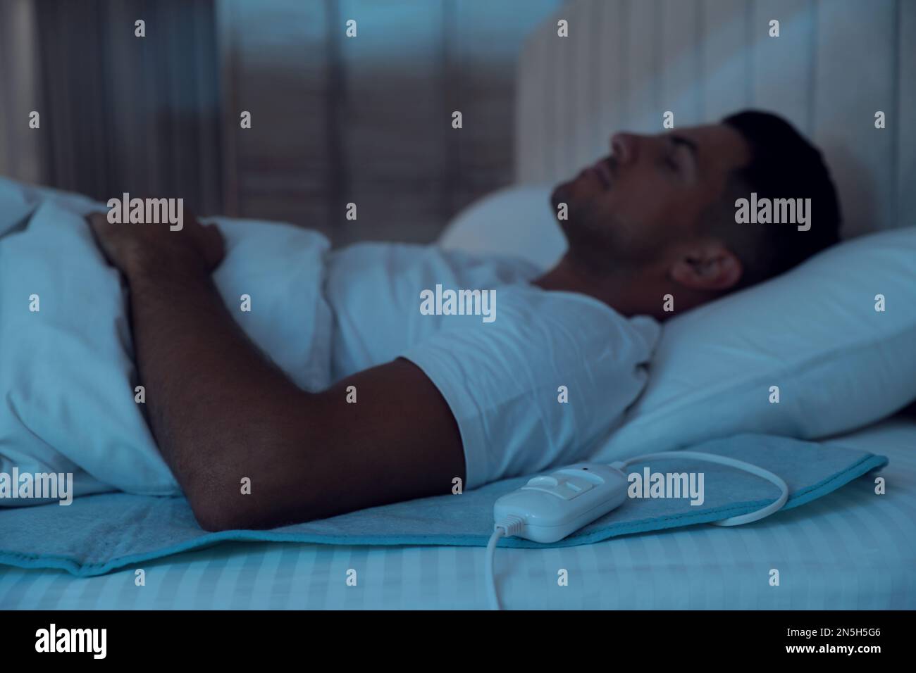 Man sleeping in bed with electric heating pad, focus on cable Stock ...