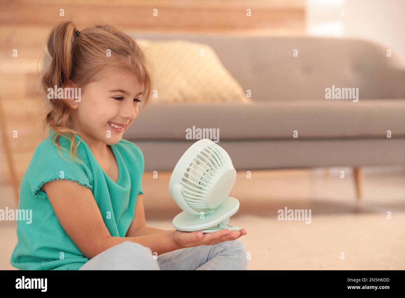 Little girl enjoying air flow from portable fan in living room. Summer ...