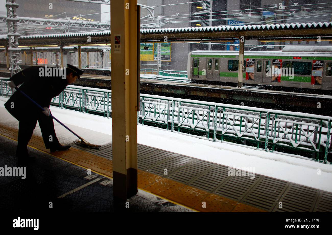 An employee of a train company sweeps snow off a train station platform ...