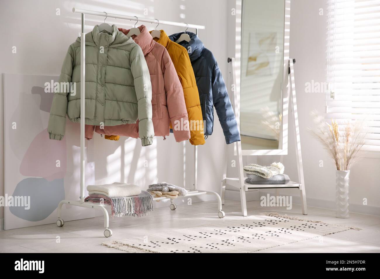 Different warm jackets on rack in stylish room interior Stock Photo - Alamy