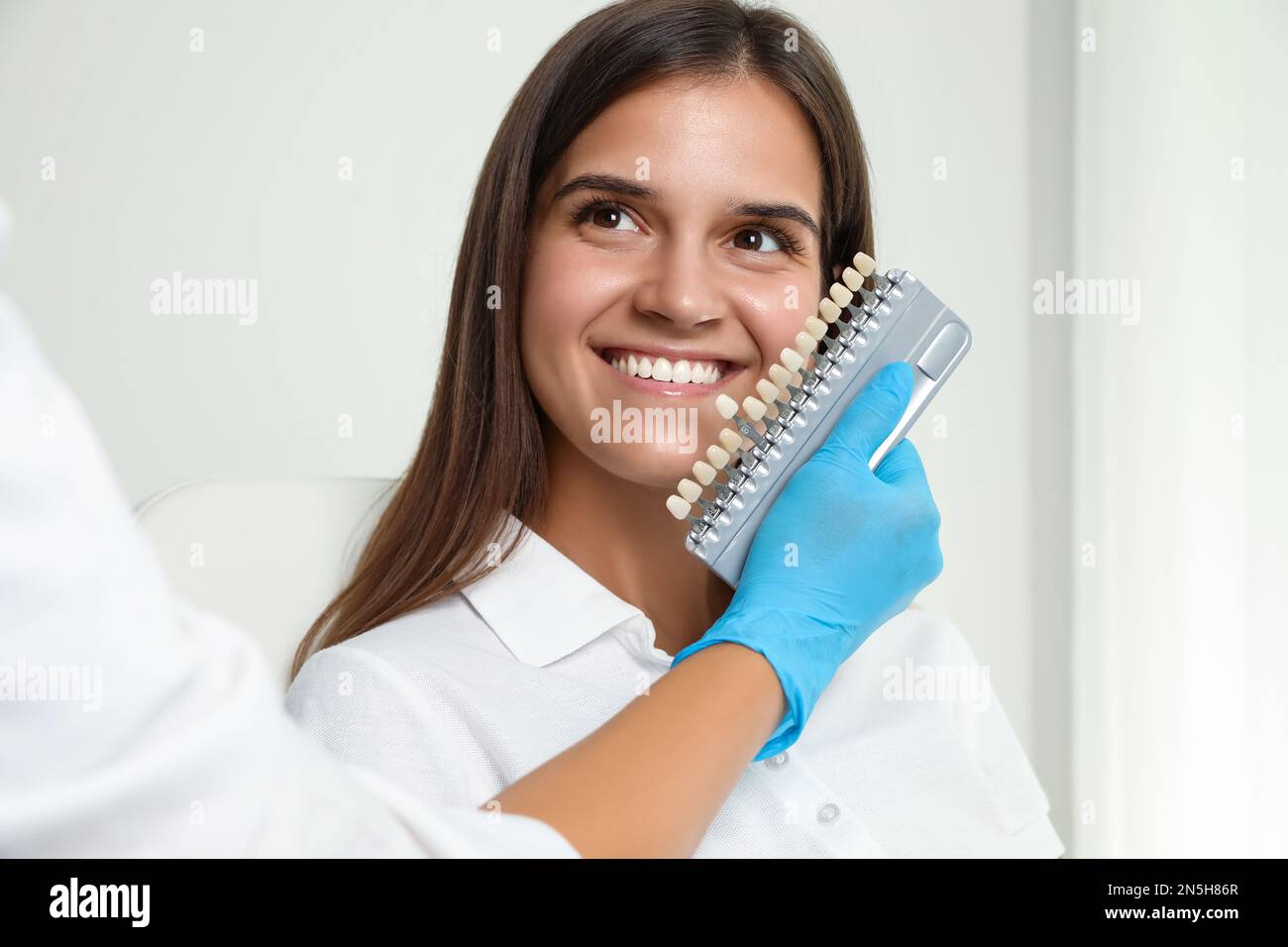 Doctor checking young woman's teeth color in clinic. Cosmetic dentistry ...