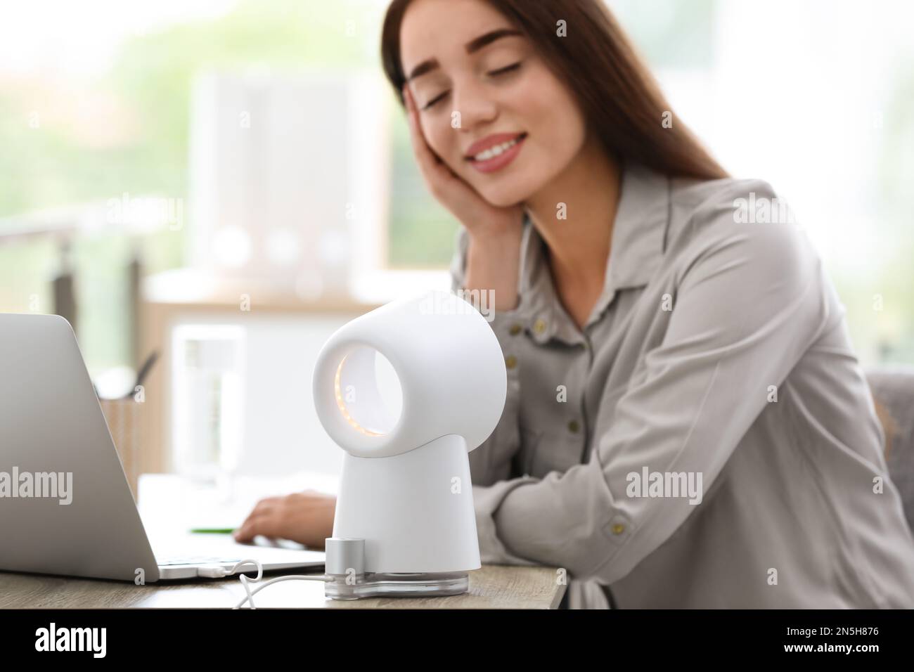 Young woman enjoying air flow from portable fan at workplace. Summer ...