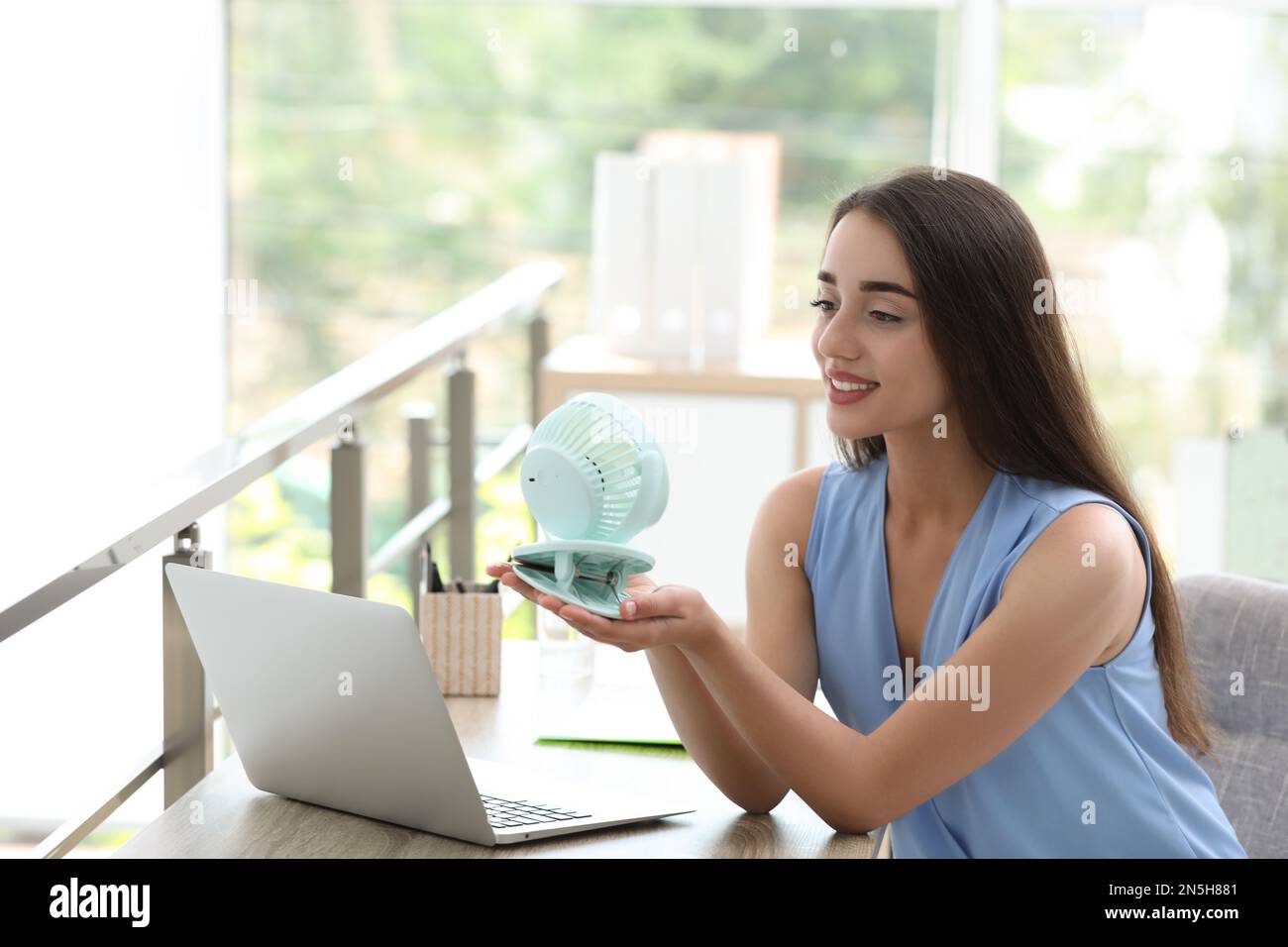 Young woman enjoying air flow from portable fan at workplace. Summer ...