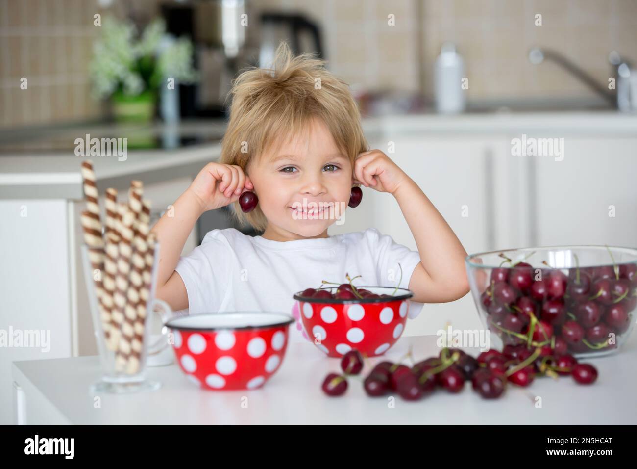 Cute blond child, toddler boy, eating cherries at home, having fun ...