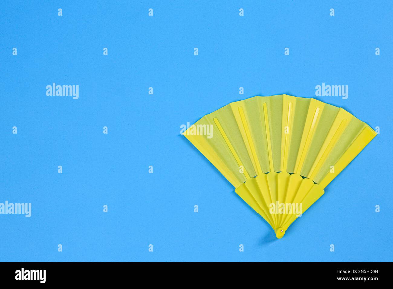 Yellow hand fan on light blue background, top view. Space for text ...