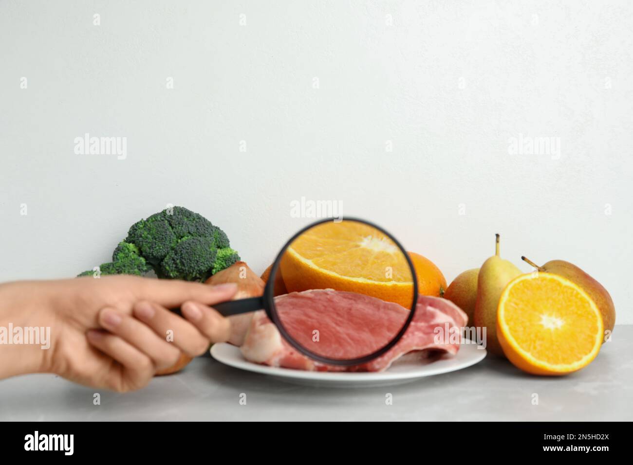 Woman with magnifying glass exploring raw meat and fruits, space for ...