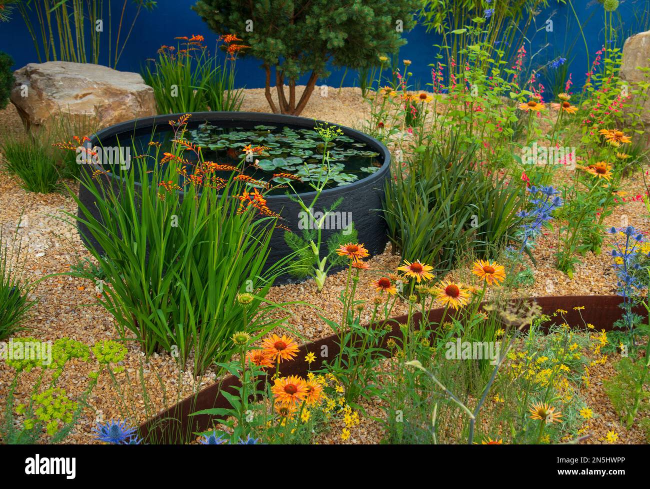 A circular water feature surrounded by gravel and colourful perennials ...