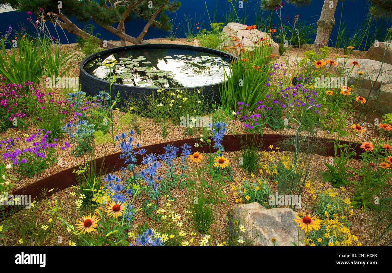 A circular water feature surrounded by gravel and colourful perennials ...