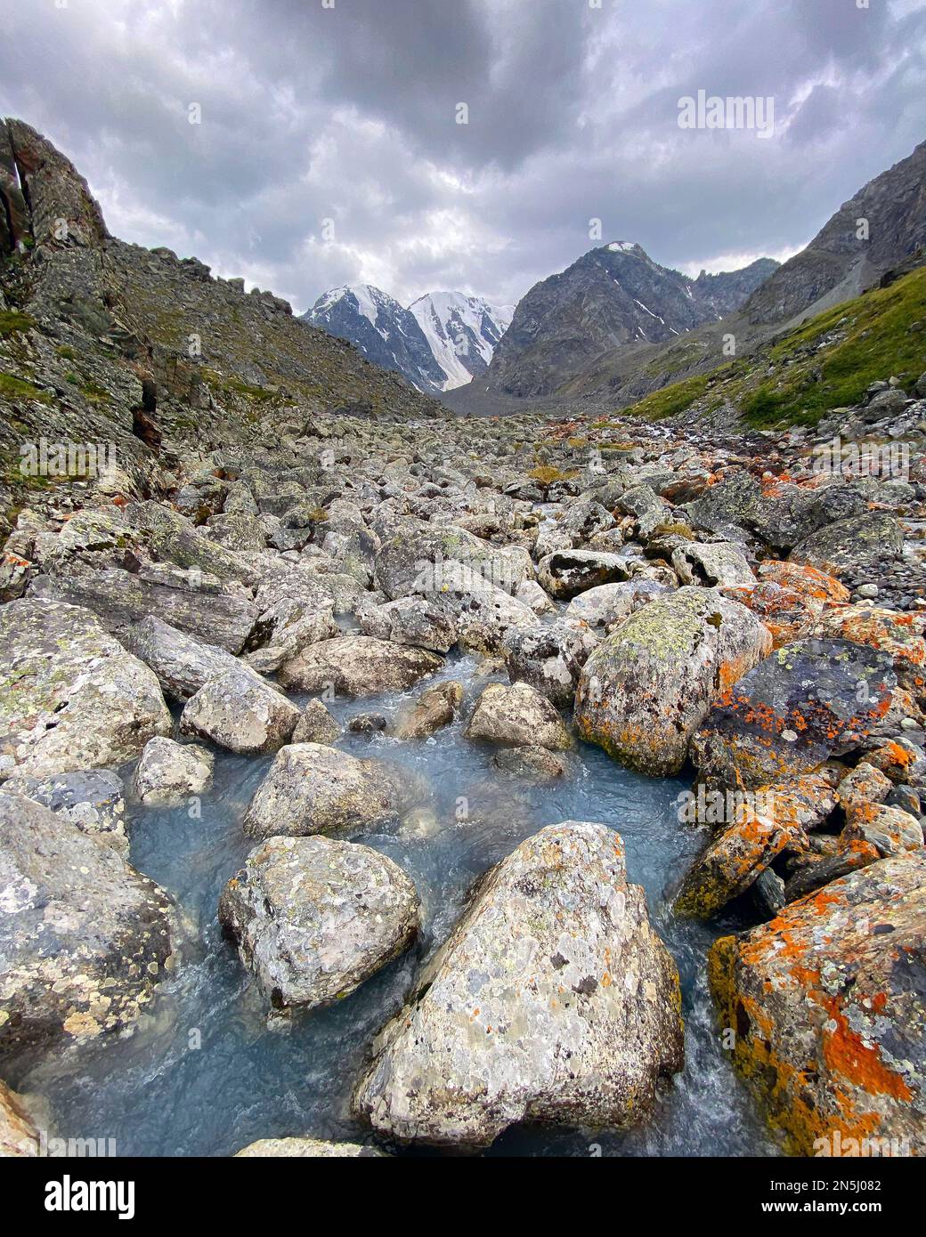 Alpine river flows over stones with orange moss from mountains with ...