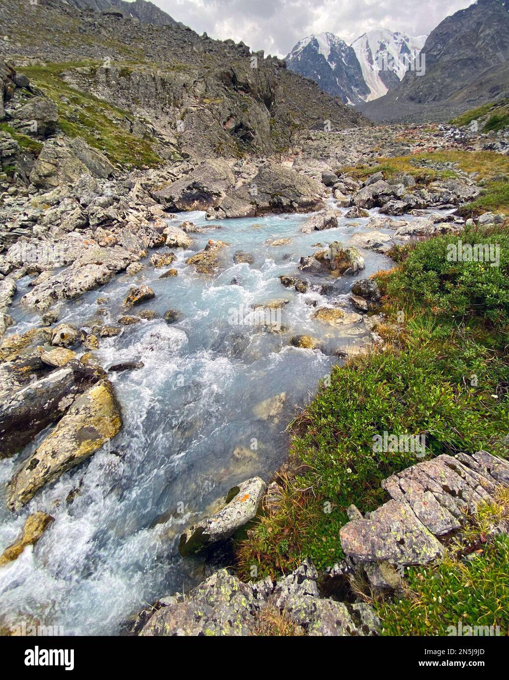 Alpine river flows over stones from mountains with glaciers and snow in ...