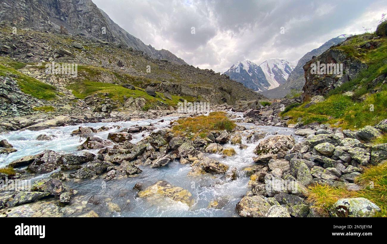 Alpine river flows over stones from mountains with glaciers and snow in ...