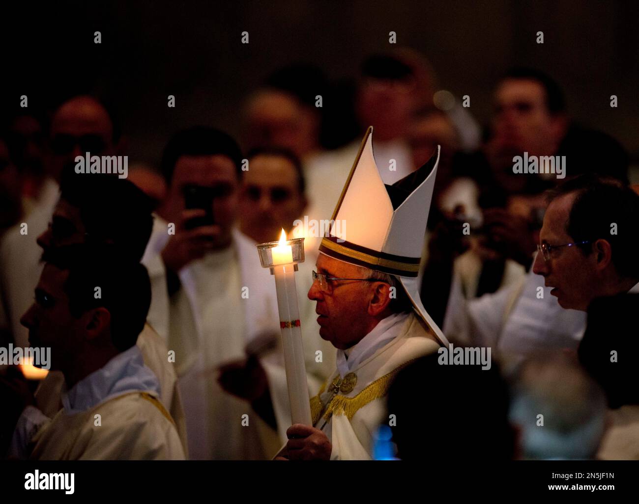 Pope Francis holds a candle as he arrives for a mass for priests and ...