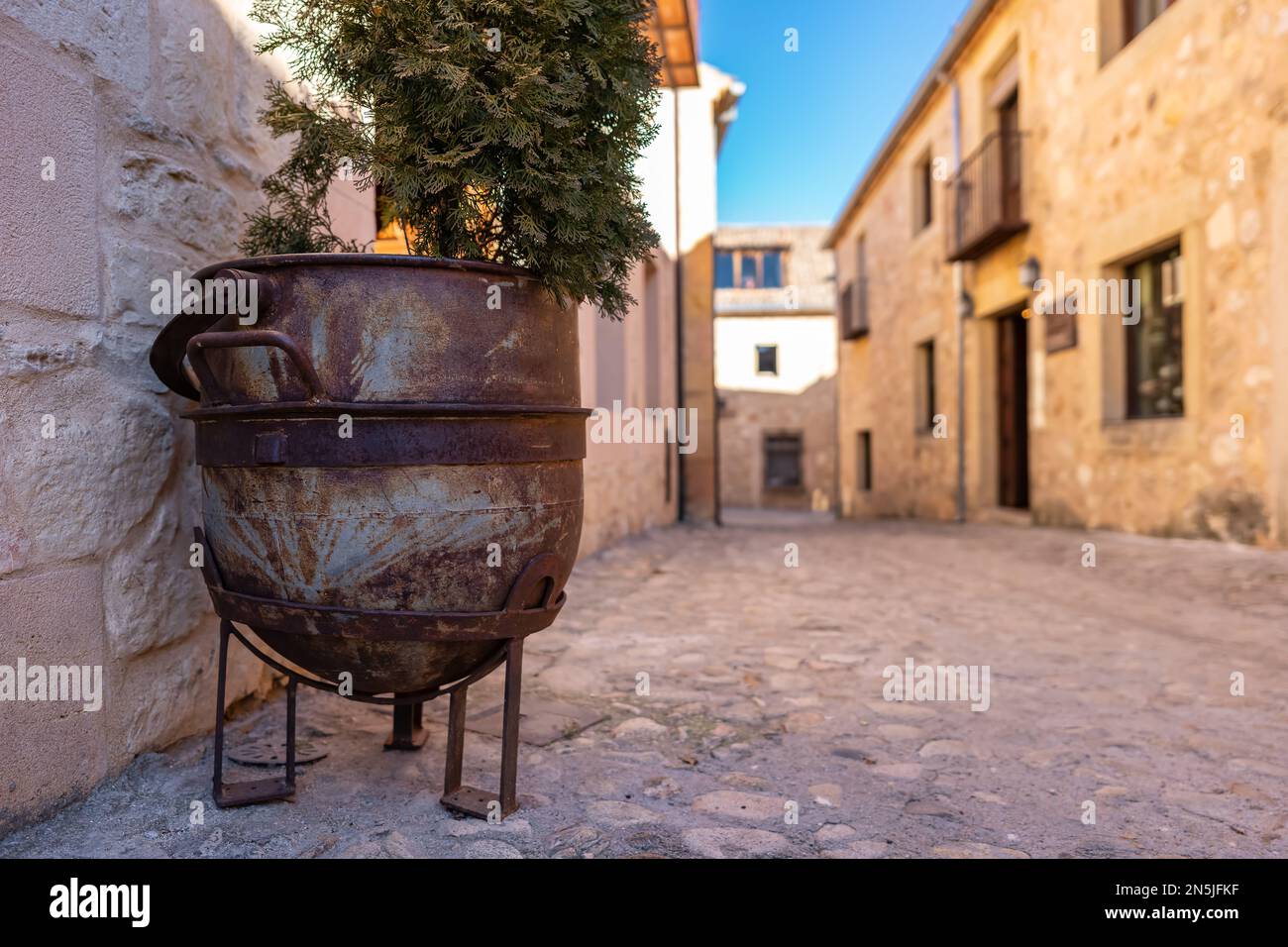 Medieval alley with stone houses and iron pot with decorative green ...