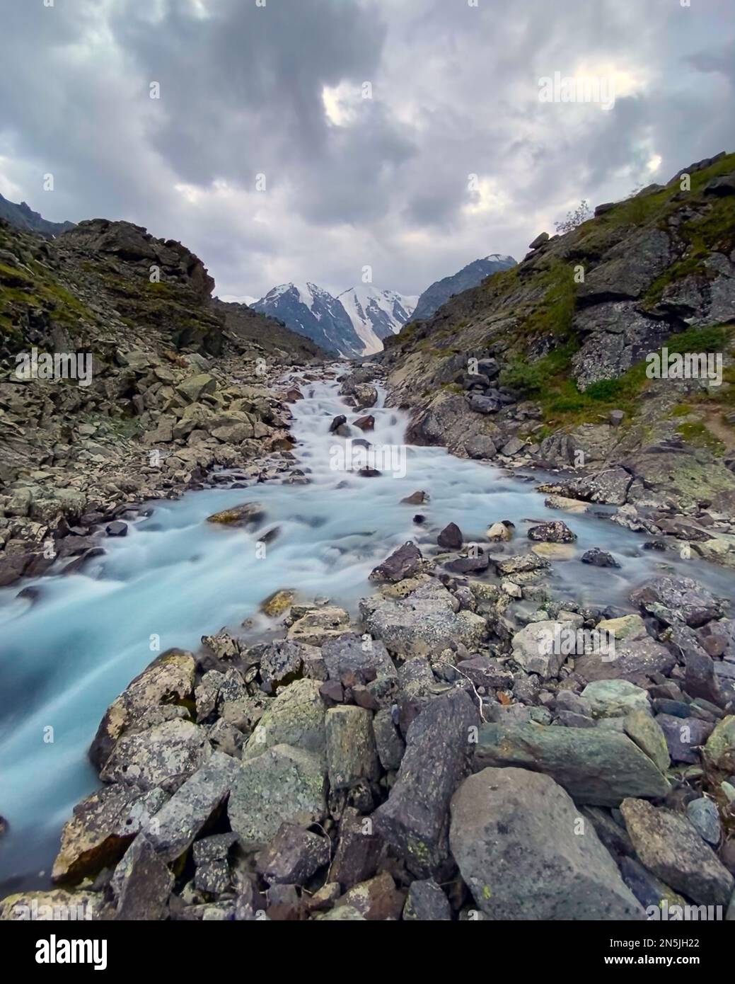 Alpine river flows over stones from mountains with glaciers and snow in ...