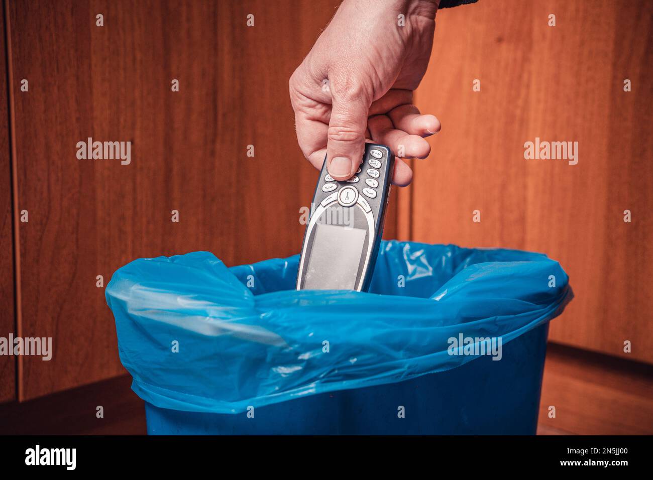 A man throws an old mobile phone into the trash. Man's hand with a ...