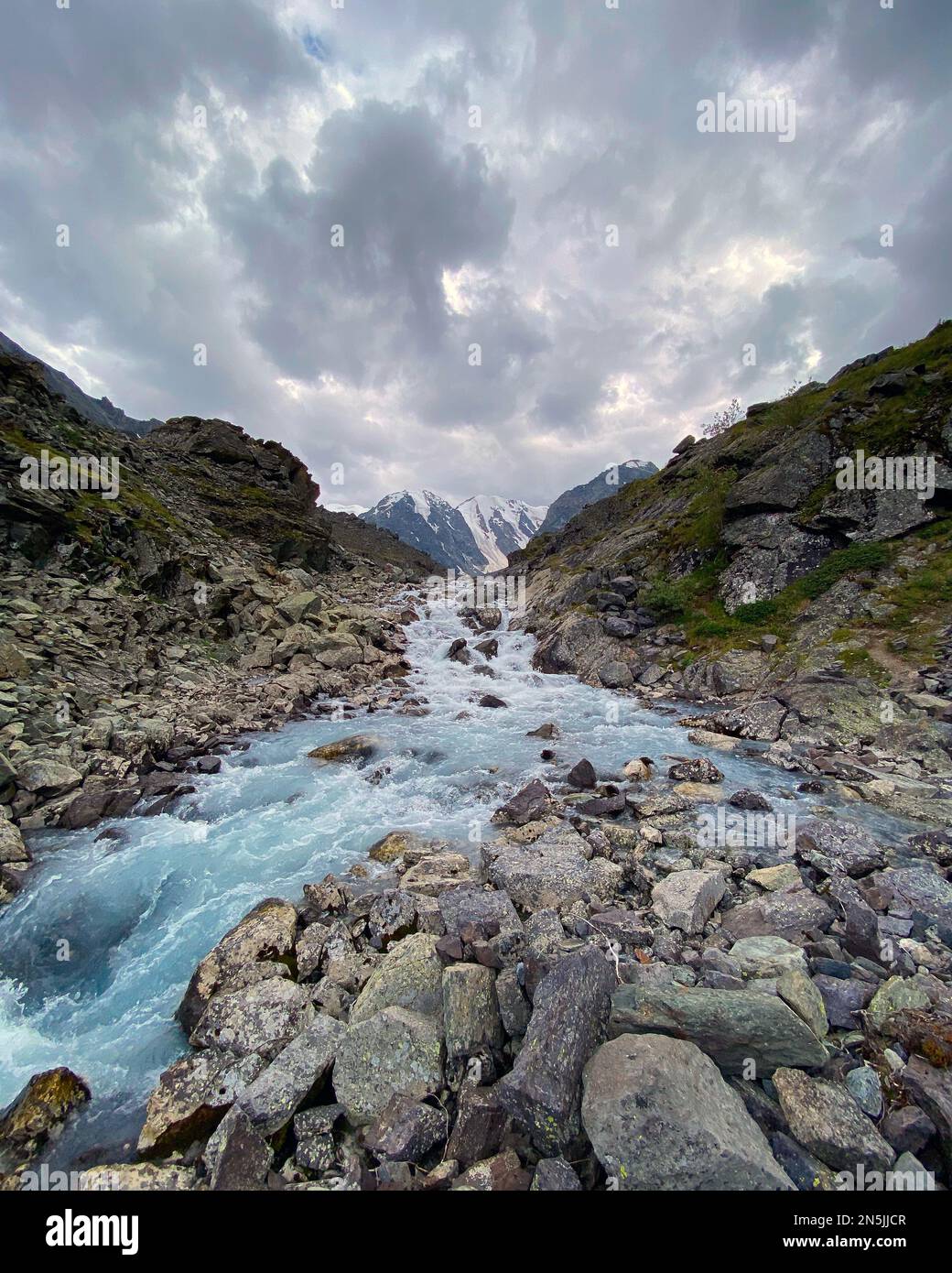 Alpine river flows over stones from mountains with glaciers and snow in ...