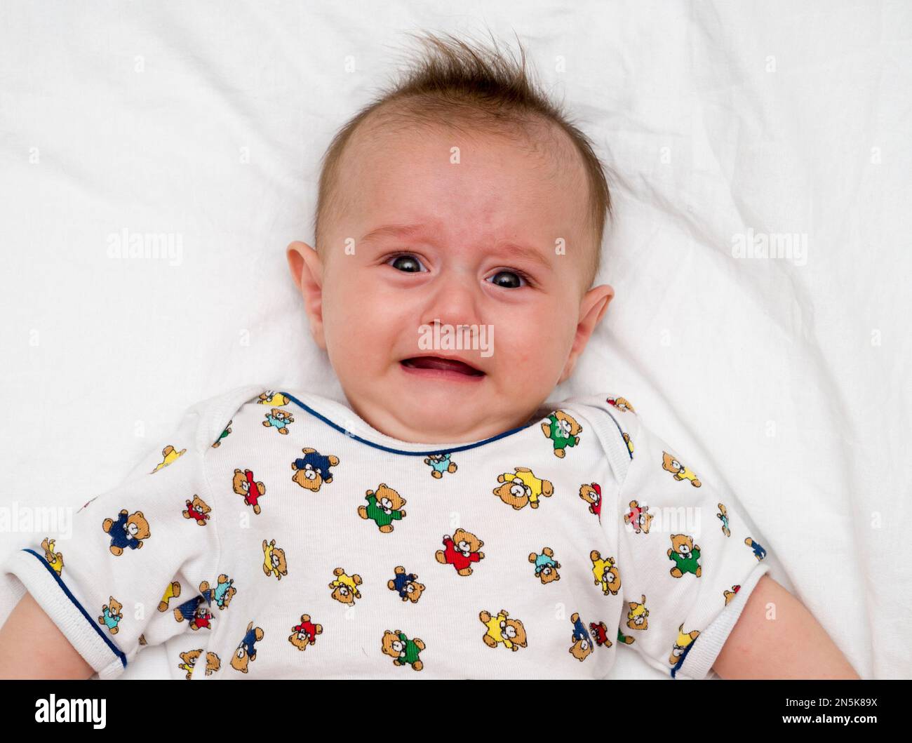 Crying baby lies on a white fluffy background Stock Photo - Alamy