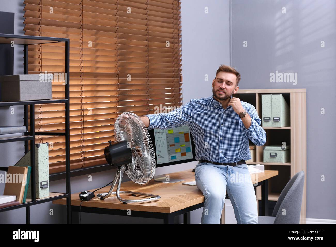 Man enjoying air flow from fan at workplace Stock Photo - Alamy