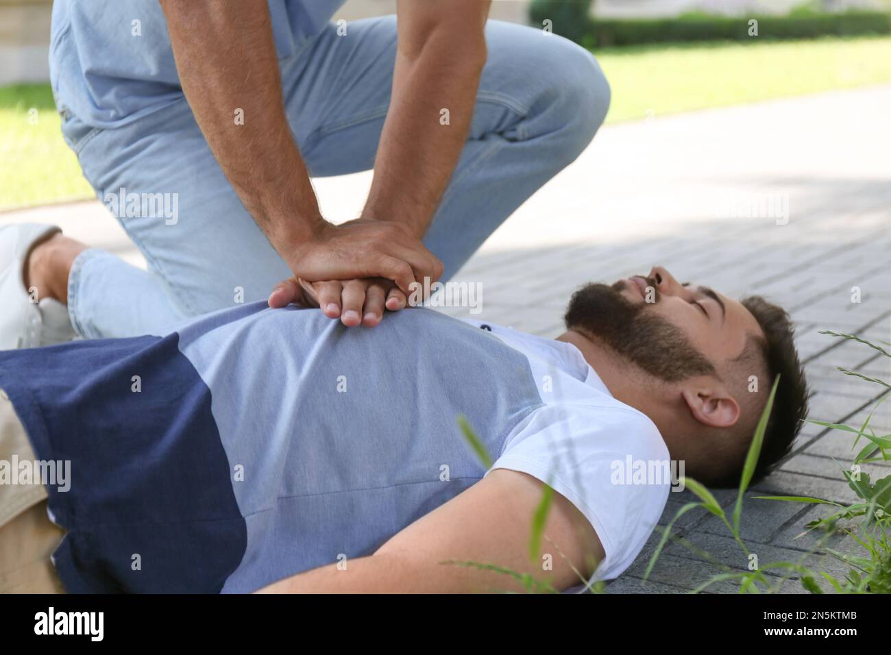 Passerby performing CPR on unconscious young man in park. First aid ...