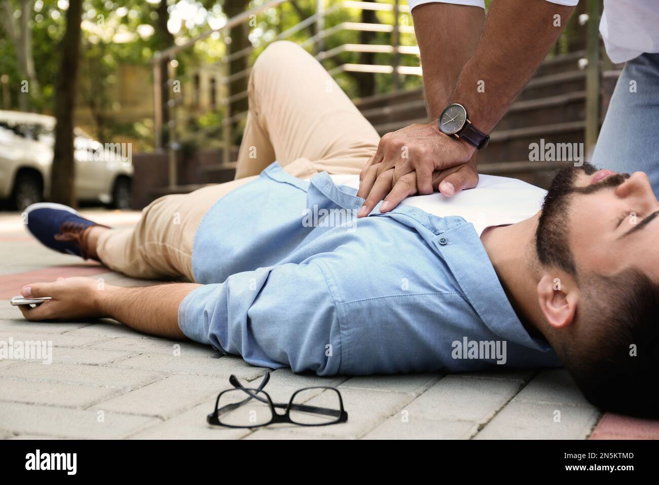Passerby performing CPR on unconscious young man outdoors. First aid ...