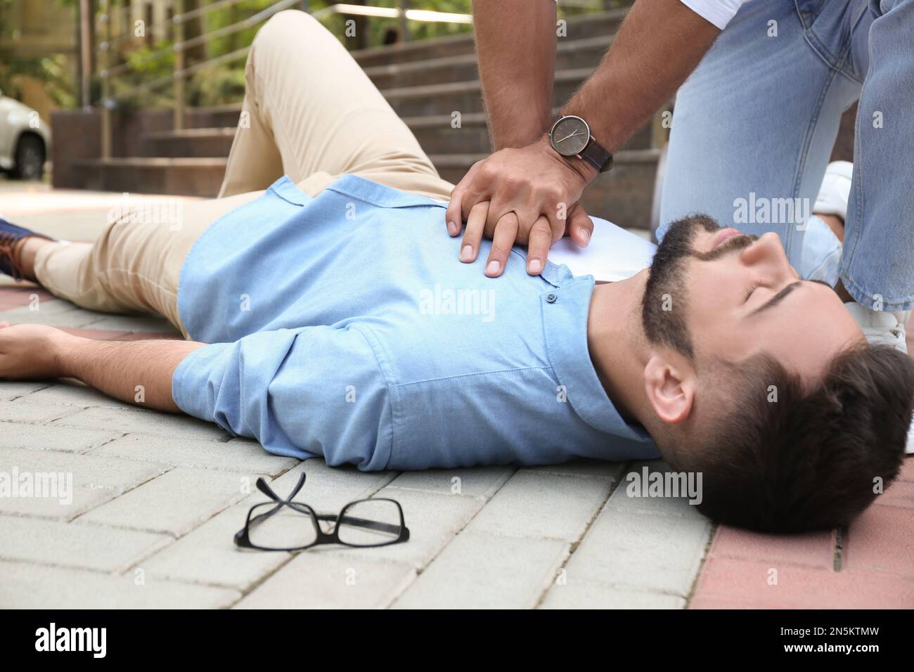 Passerby performing CPR on unconscious young man outdoors. First aid ...