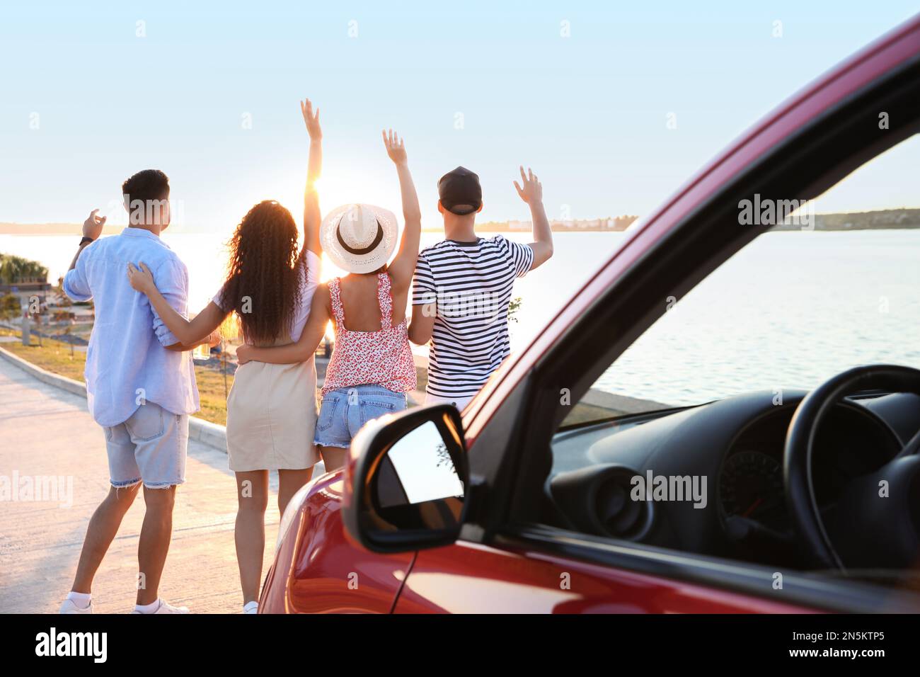 Group of friends near car outdoors at sunset, back view. Summer trip ...