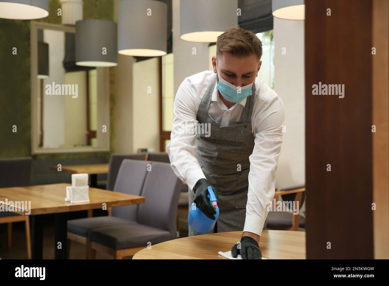 Waiter cleaning table with rag and detergent in restaurant. Surface ...